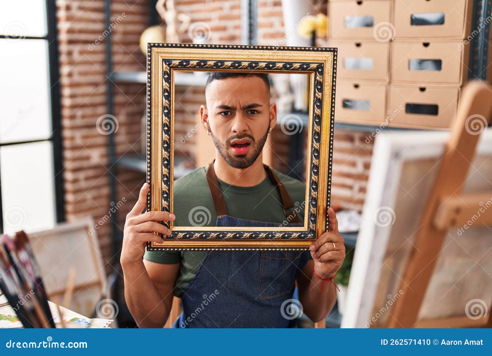 Young Hispanic Man Sitting at Art Studio with Empty Frame Clueless and ...