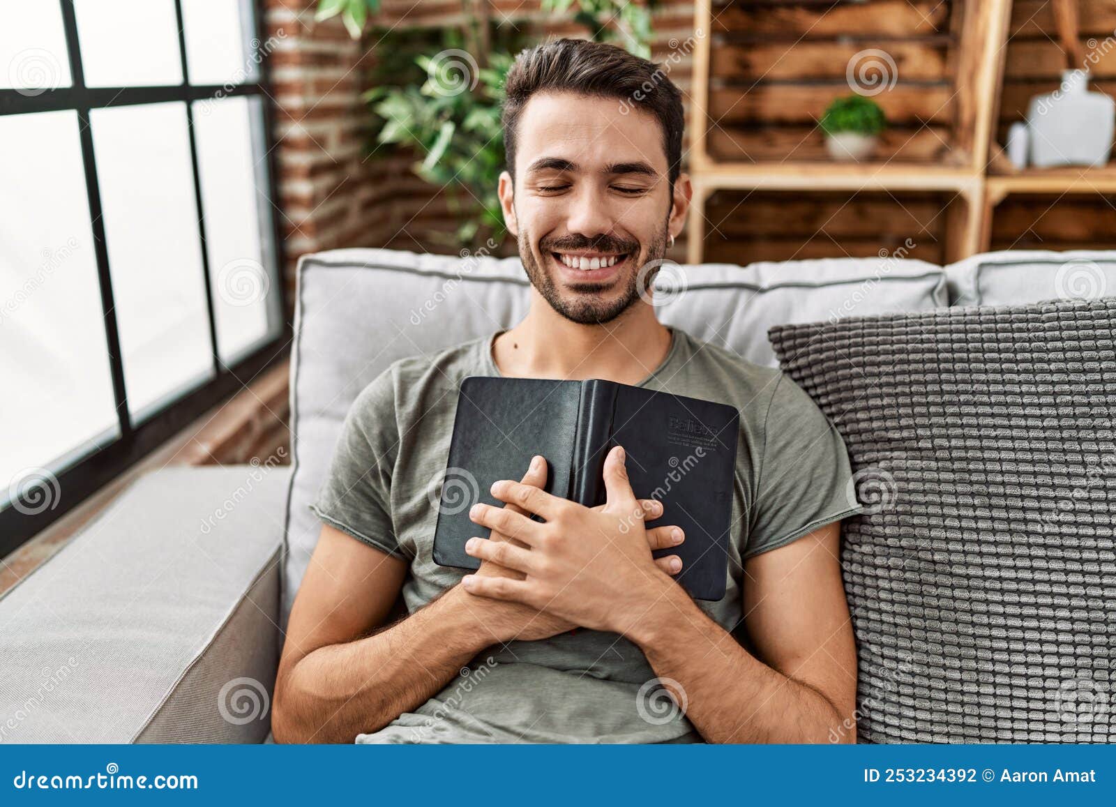 Young Hispanic Man Smiling Confident Hugging Bible at Home Stock Photo ...