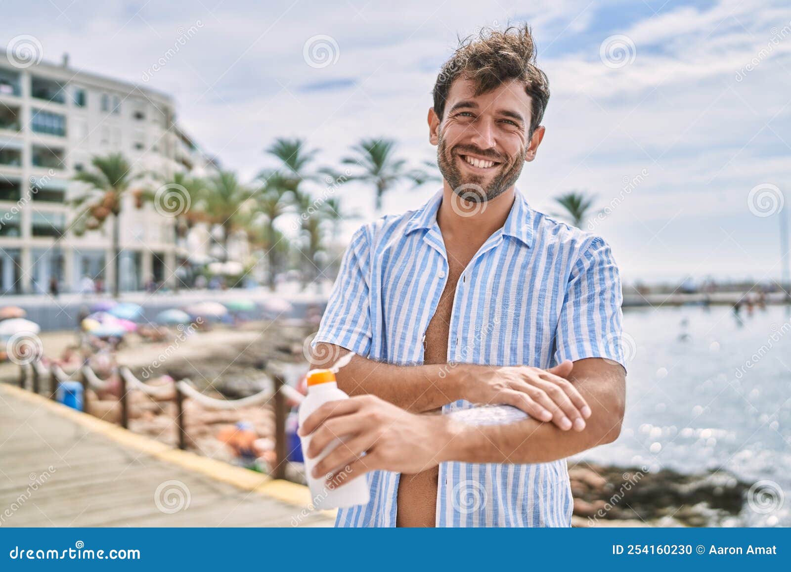 Young Hispanic Man Smiling Happy Using Sunscreen Lotion at the Beach ...