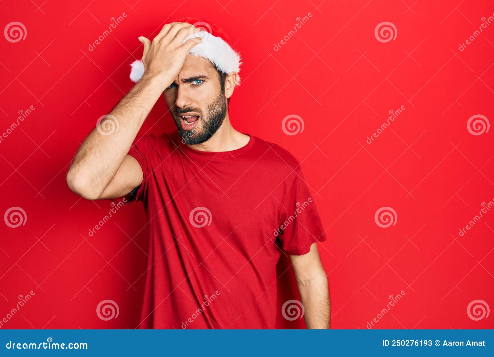 Young Hispanic Man Wearing Christmas Hat Surprised with Hand on Head ...