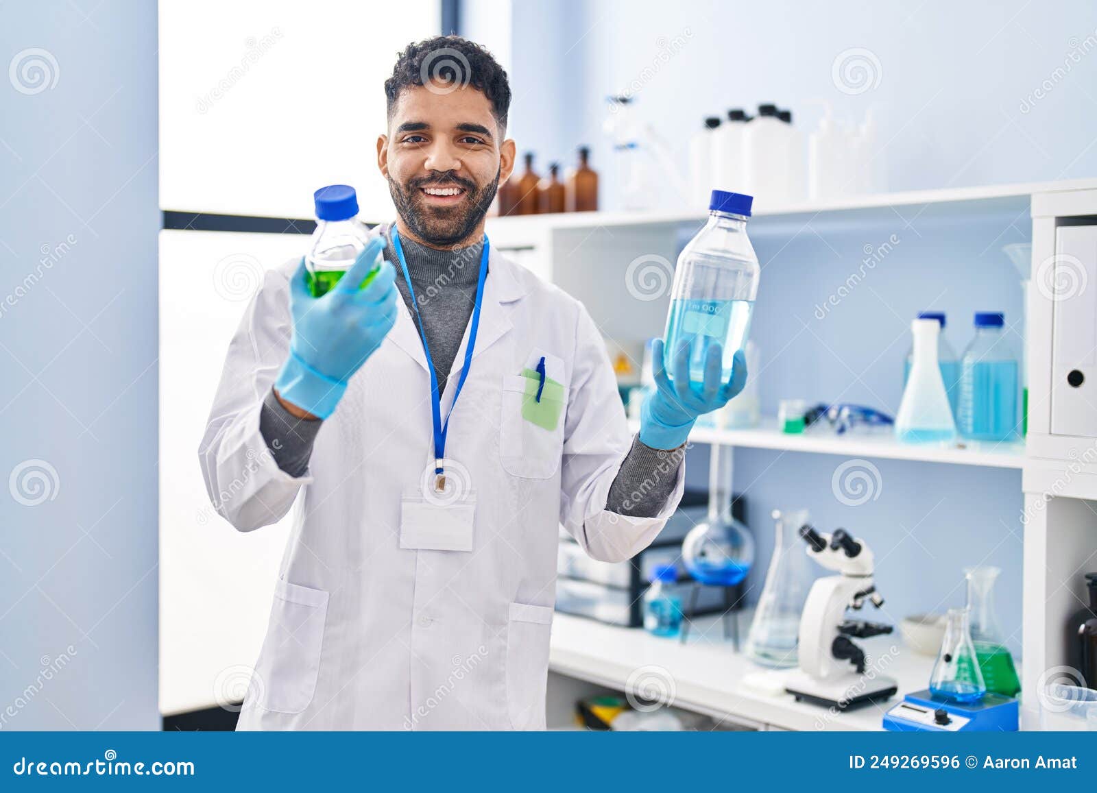 Young Hispanic Man Wearing Scientist Uniform Holding Bottles at ... Young Hispanic Man Wearing Scientist Uniform Holding Bottles at ...