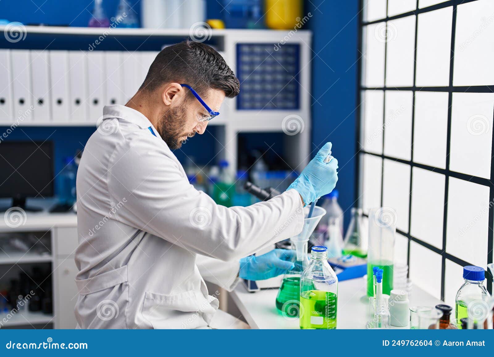 Young Hispanic Man Wearing Scientist Uniform Measuring Liquid at ... Young Hispanic Man Wearing Scientist Uniform Measuring Liquid at ...