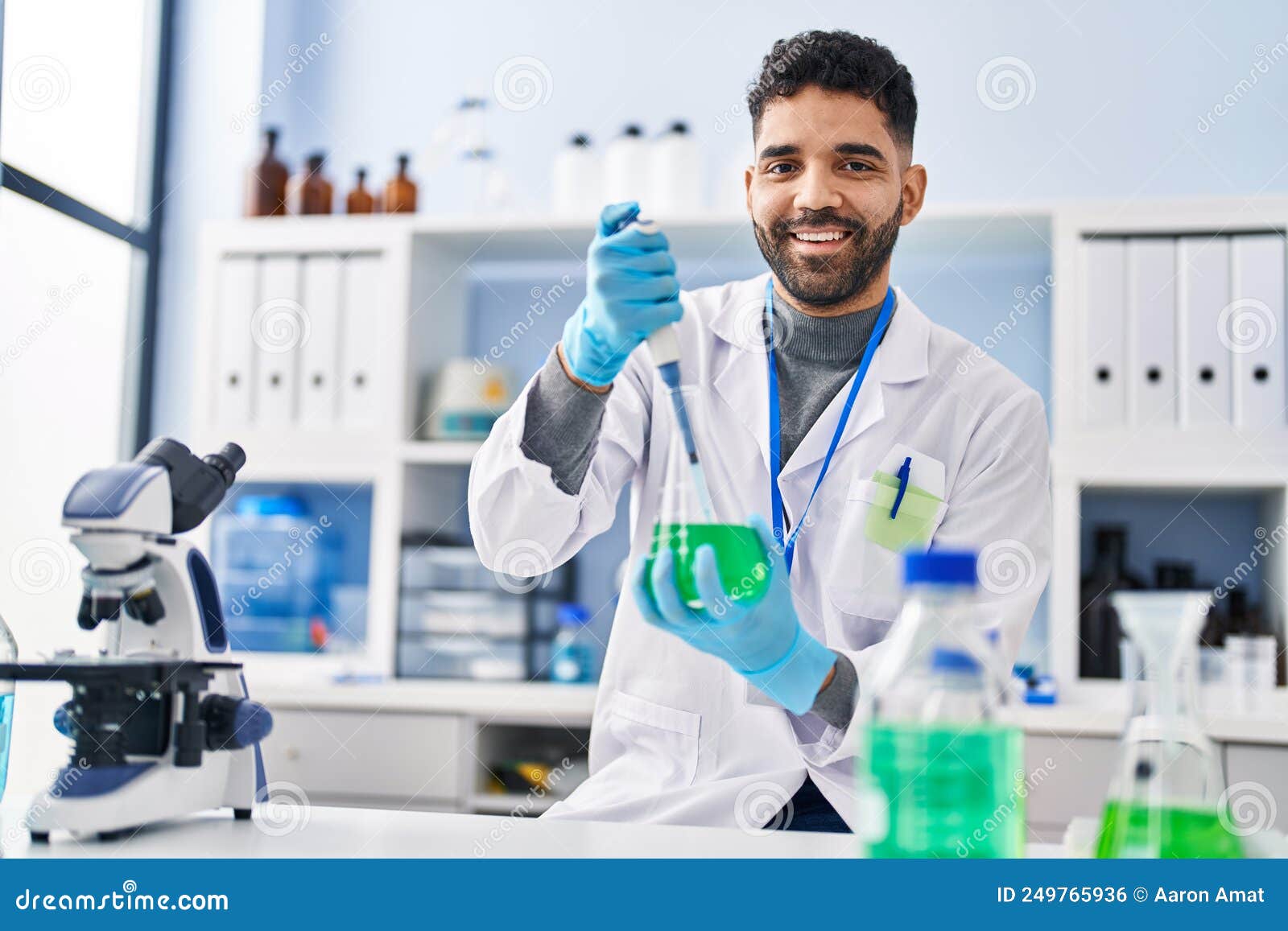 Young Hispanic Man Wearing Scientist Uniform Measuring Liquid at ... Young Hispanic Man Wearing Scientist Uniform Measuring Liquid at ...