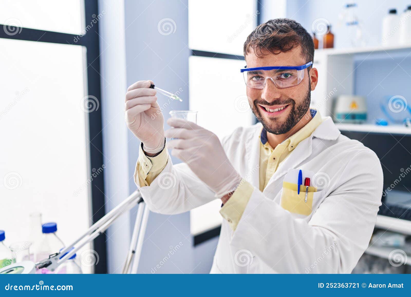 Young Hispanic Man Wearing Scientist Uniform Measuring Liquid at ... Young Hispanic Man Wearing Scientist Uniform Measuring Liquid at ...