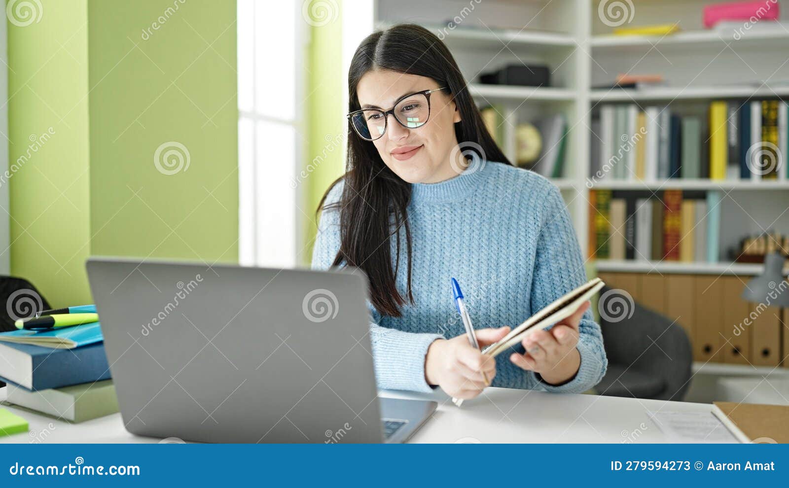 Young Hispanic Woman Student Using Computer Taking Notes at Library ...