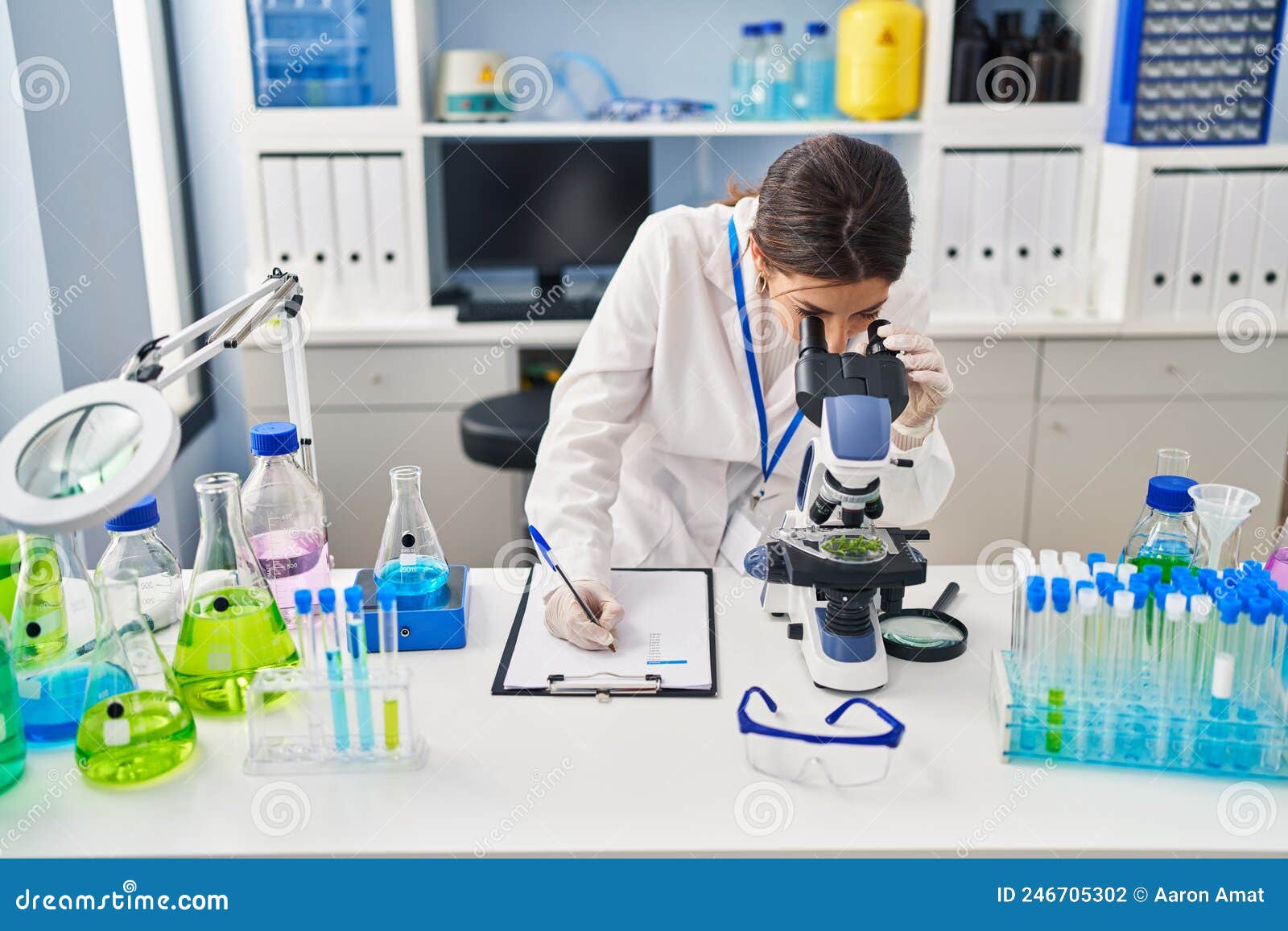 Young Hispanic Woman Wearing Scientist Uniform Using Microscope and ...