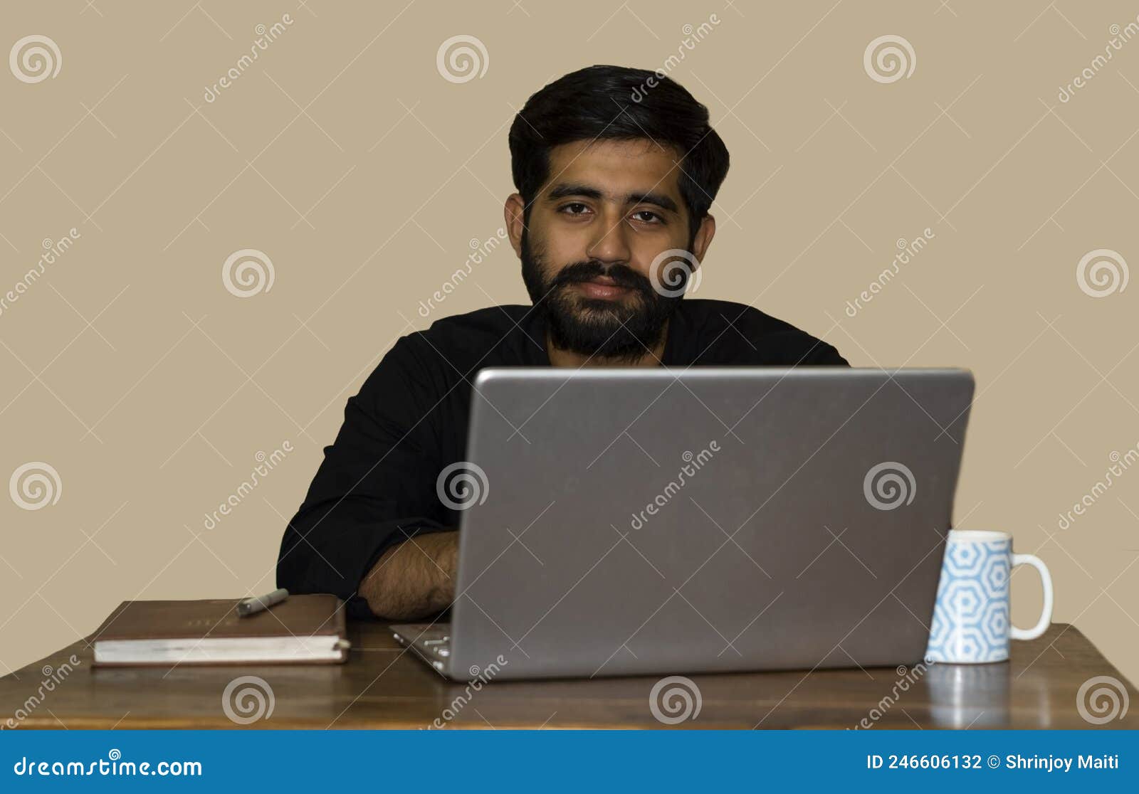 A Young Indian Man Looking at the Camera while Working on Laptop Stock ...