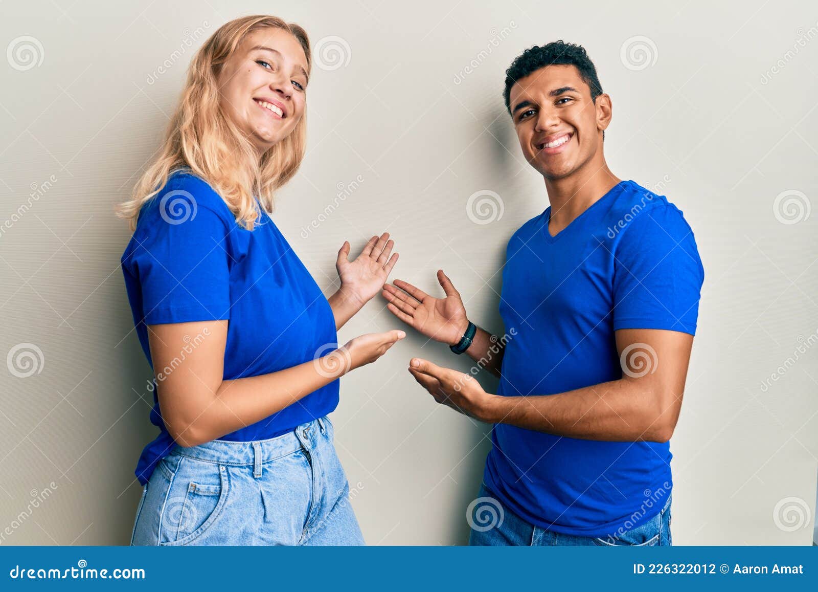 Young Interracial Couple Wearing Casual Clothes Inviting To Enter
