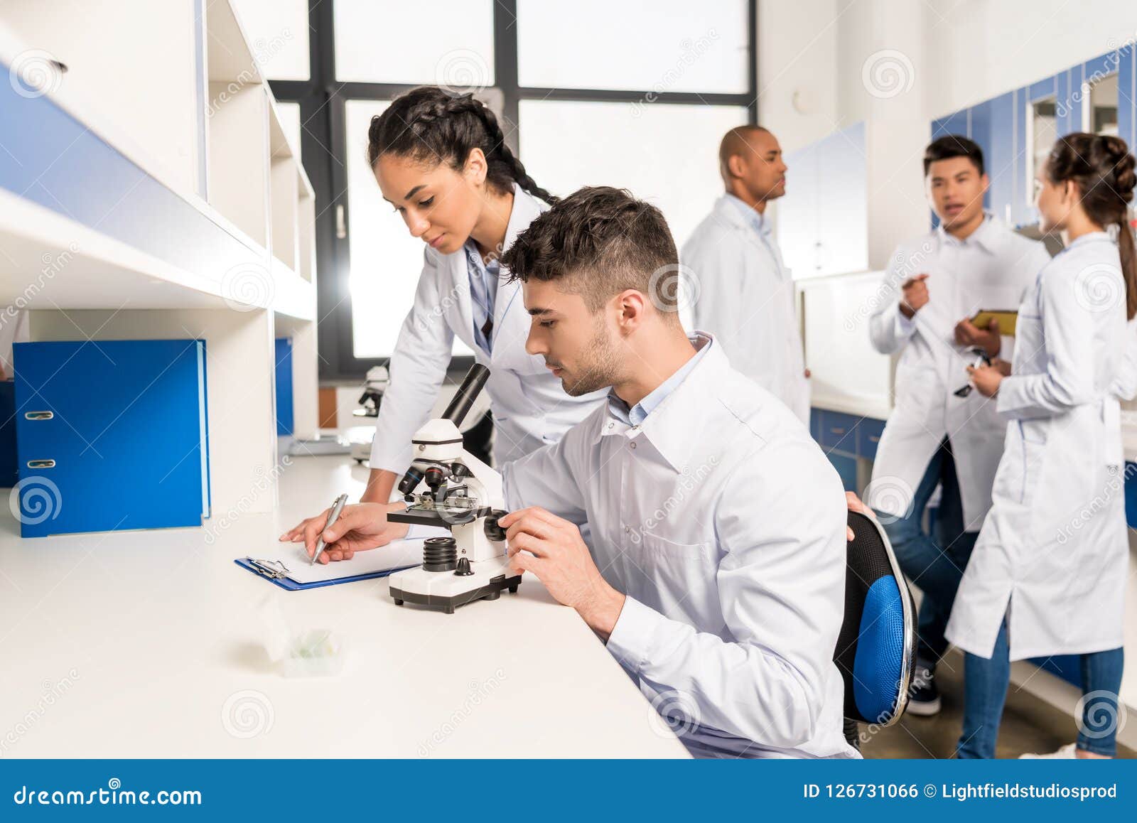 Young Lab Technicians Working with Microscope and Taking Notes on ...