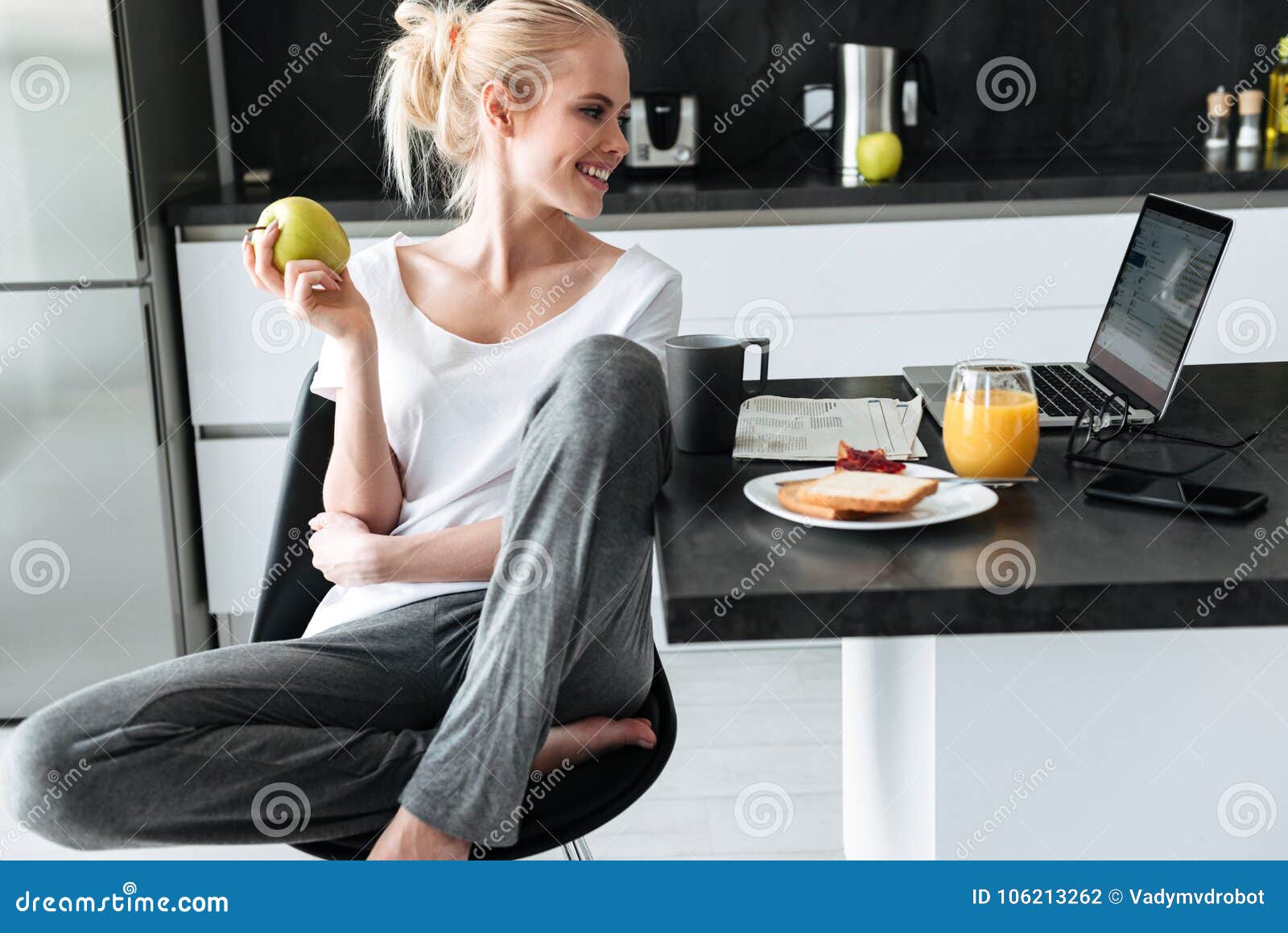 Young Lady Eating Apple and Using Laptop in Kitchen Stock Photo - Image ...