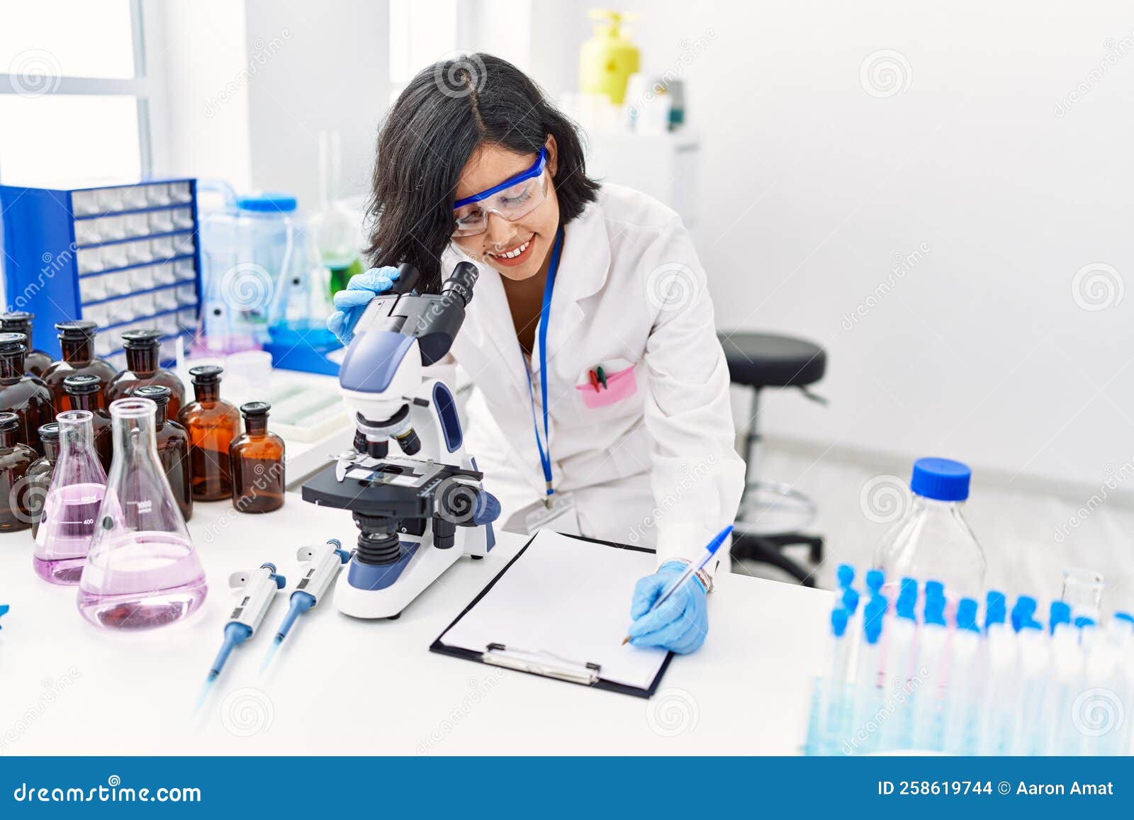 Young Latin Woman Wearing Scientist Uniform Using Microscope Write on ...