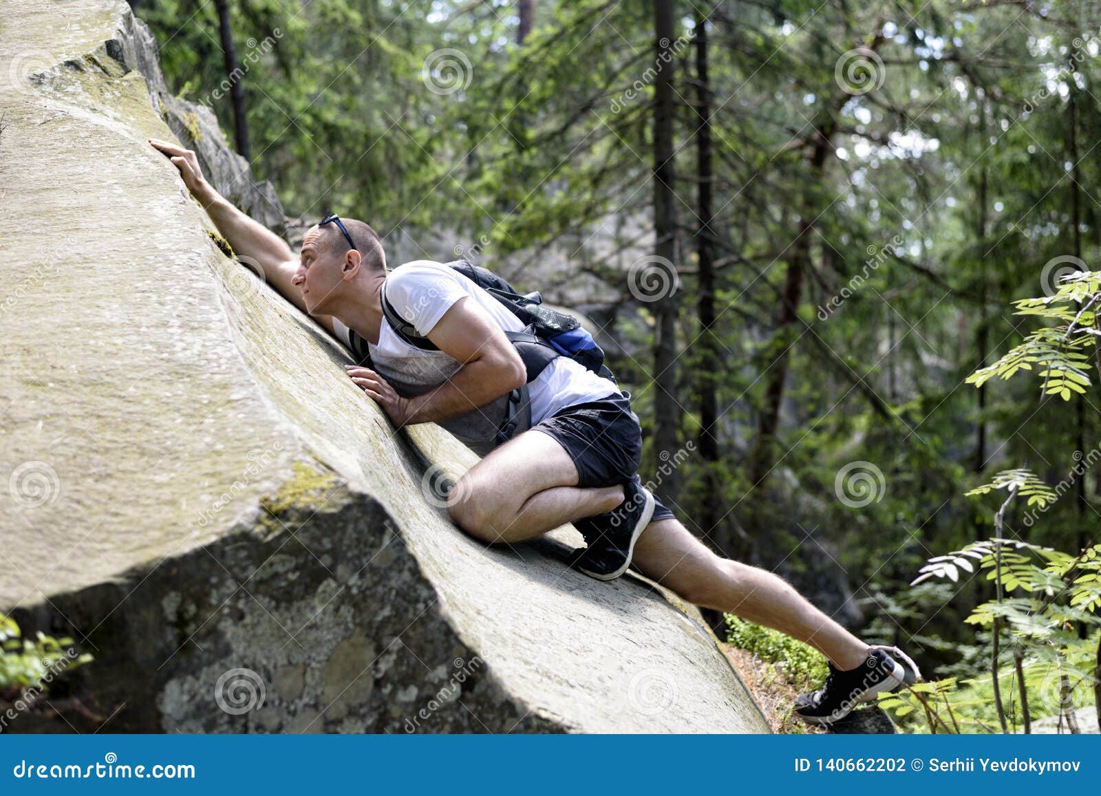 Young Man with a Backpack Climbs Up the Cliff in the Coniferous Forest ...