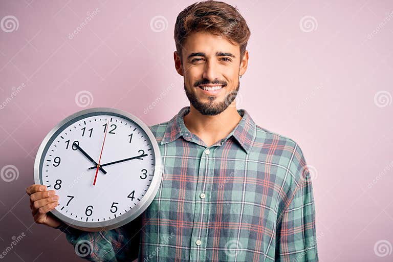 Young Man with Beard Doing Countdown Using Big Clock Over Isolated Pink ...