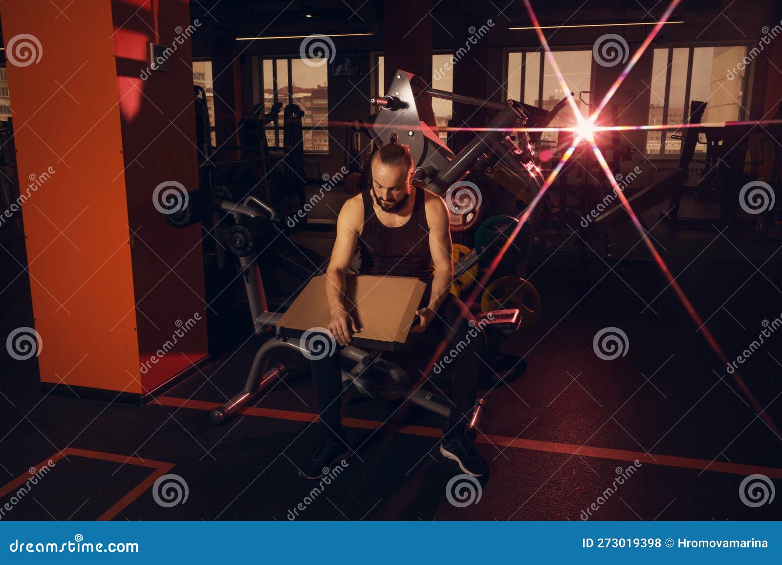 A Young Man with a Beard with a Happy Face Opens a Pizza Box in the Gym ...