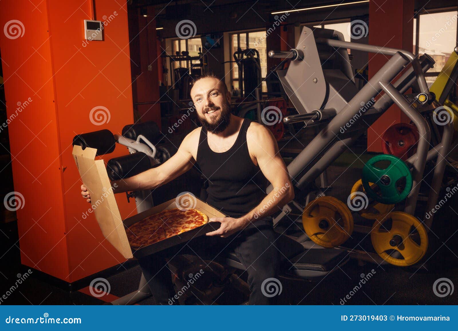 A Young Man with a Beard with a Happy Face Opens a Pizza Box in the Gym ...
