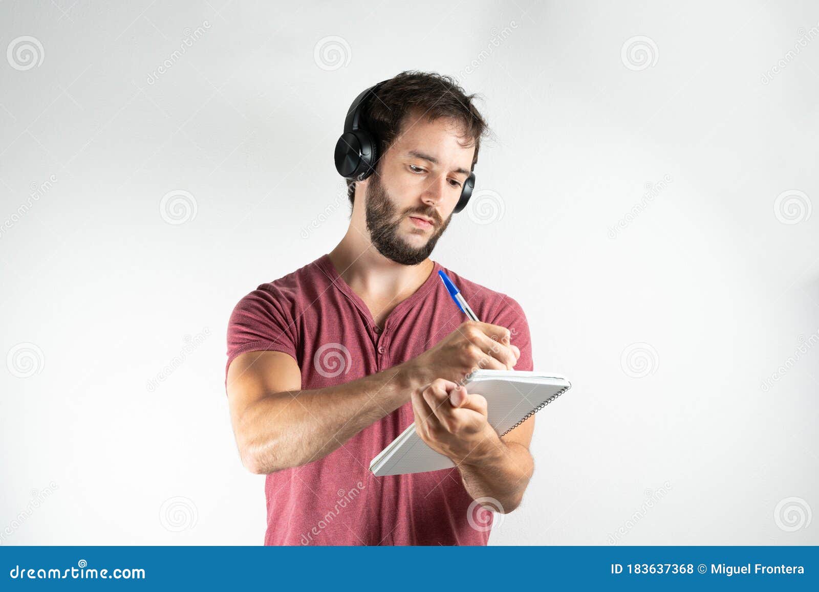 Young Man with a Beard and Wireless Headphones Taking Notes in a ...