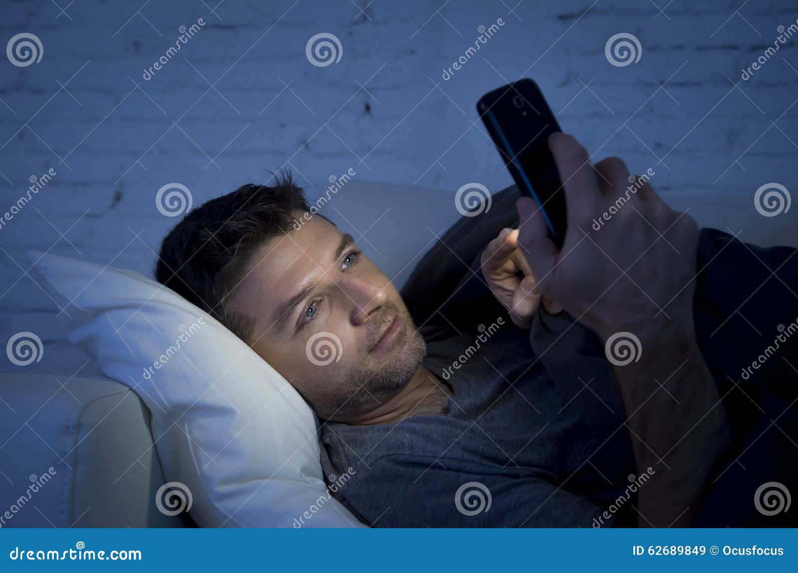 Young Man in Bed Couch at Home Late at Night Texting on Mobile Phone in ...