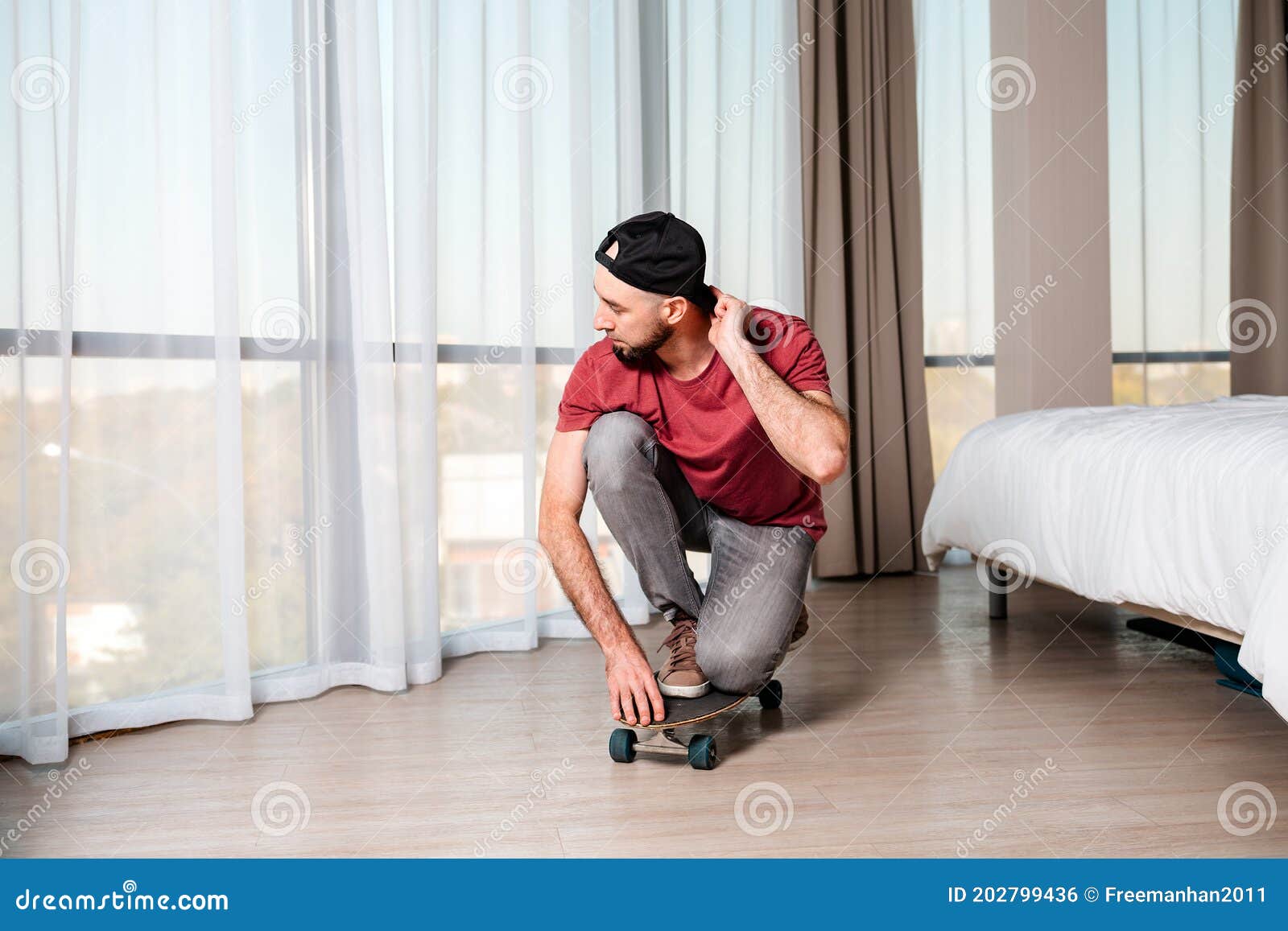 A Young Man Crouching Poses on a Longboard, Looking Out the Window ...
