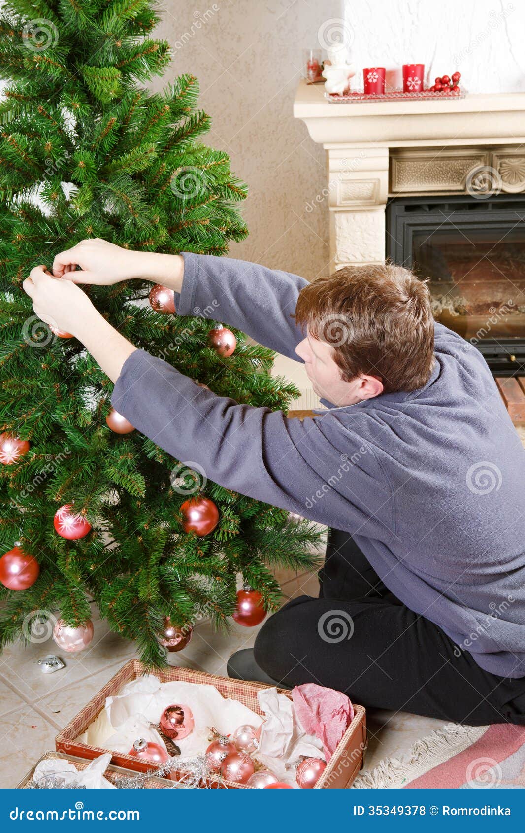 Young Man Decorating Christmas Tree at Home with Chimney. Stock Photo ...