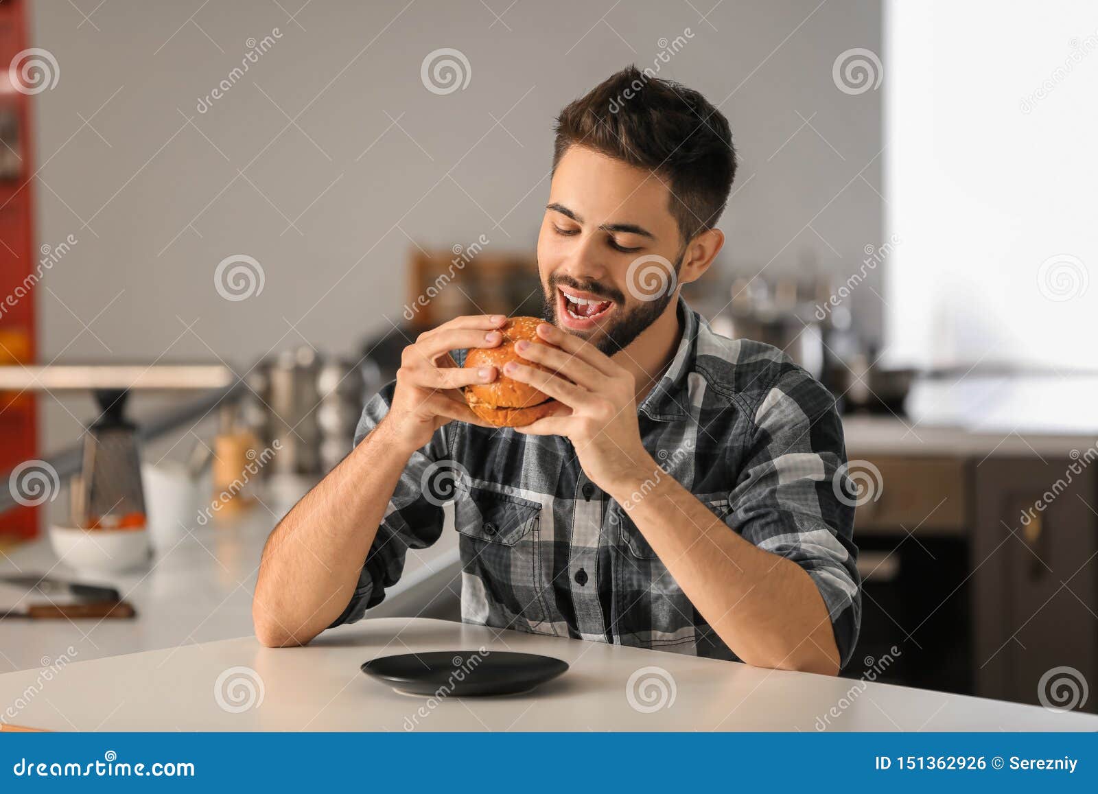 Young Man Eating Tasty Burger at Home Stock Photo - Image of hamburger ...