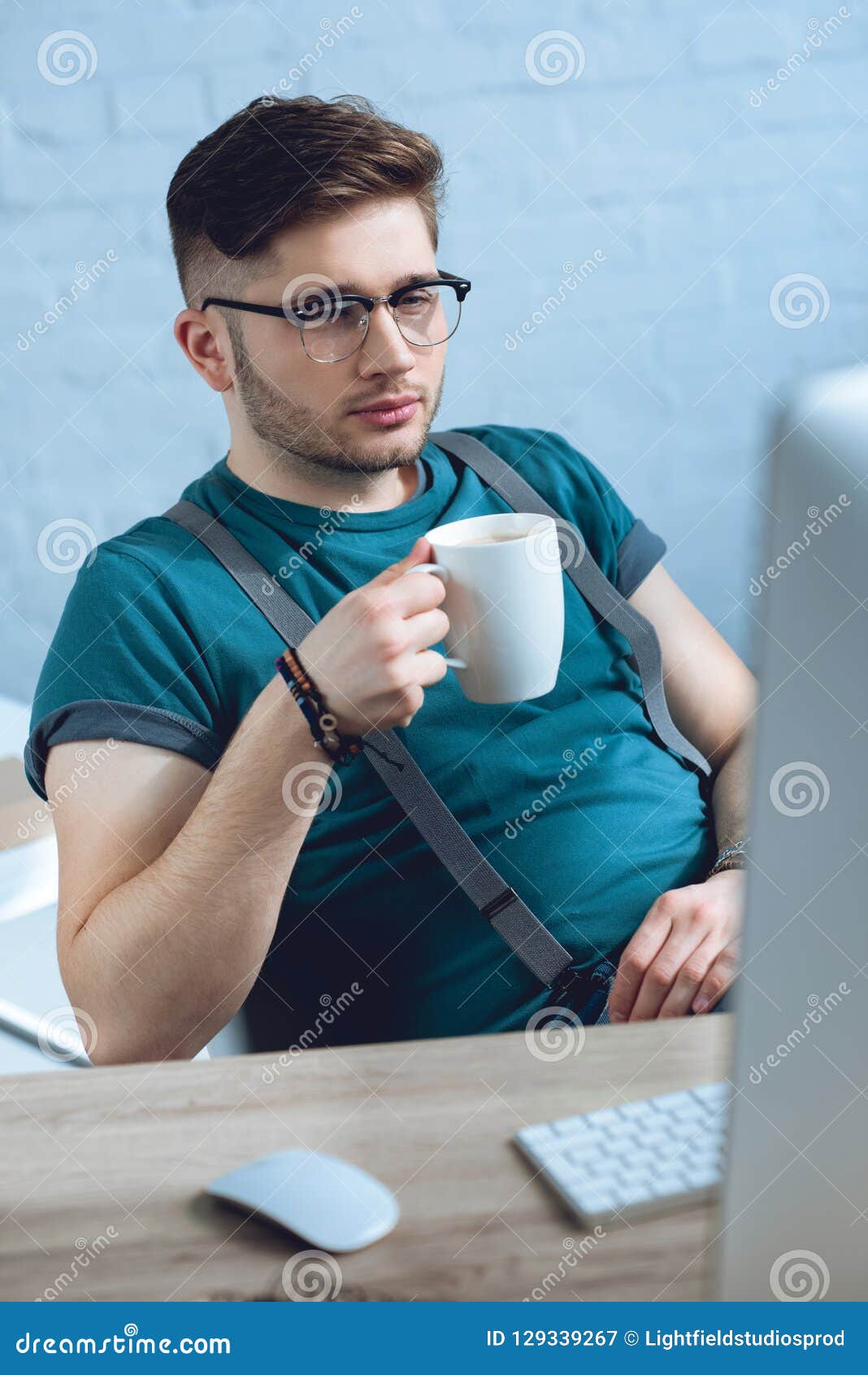 Young Man in Eyeglasses Drinking Coffee and Working with Desktop ...