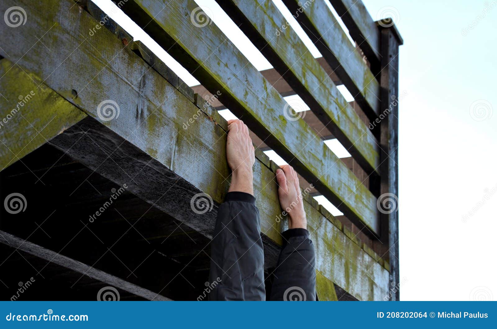 Young Man Hangs On A Wooden Railing And Tries To Step Up His Hand