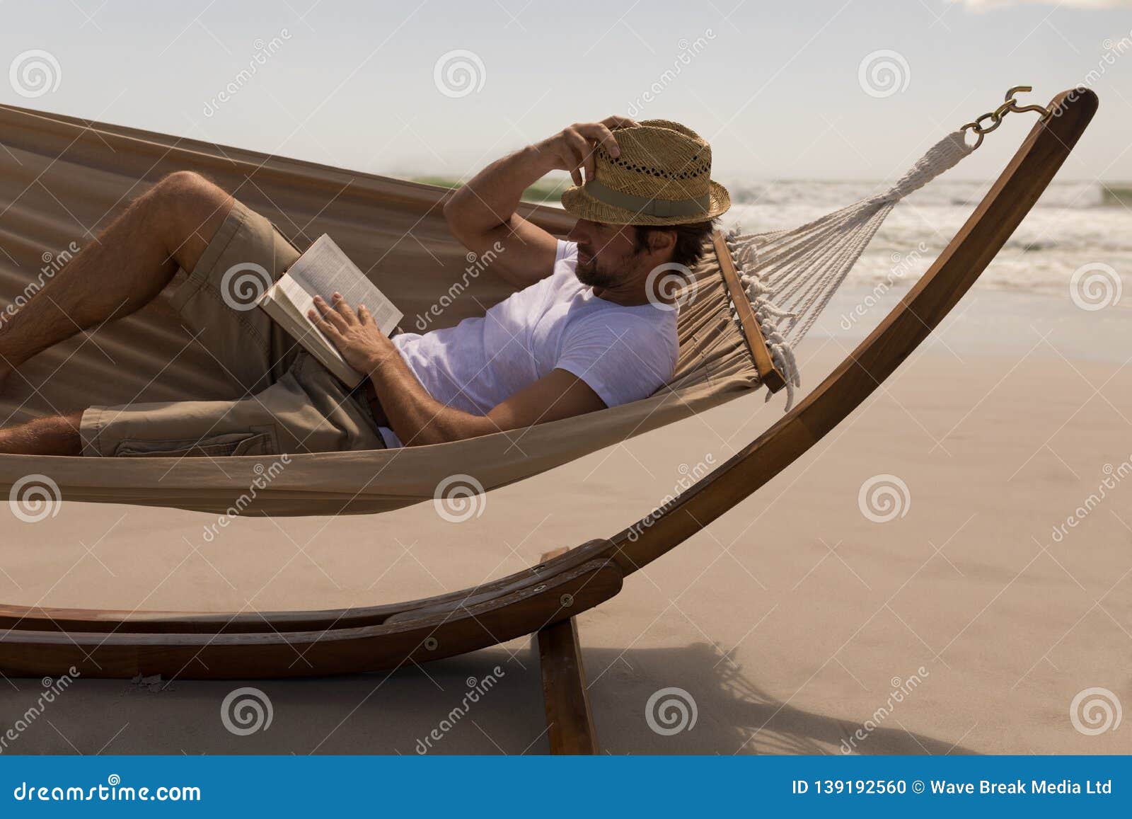 Young Man with Hat Reading a Book while Relaxing on Hammock at Beach ...