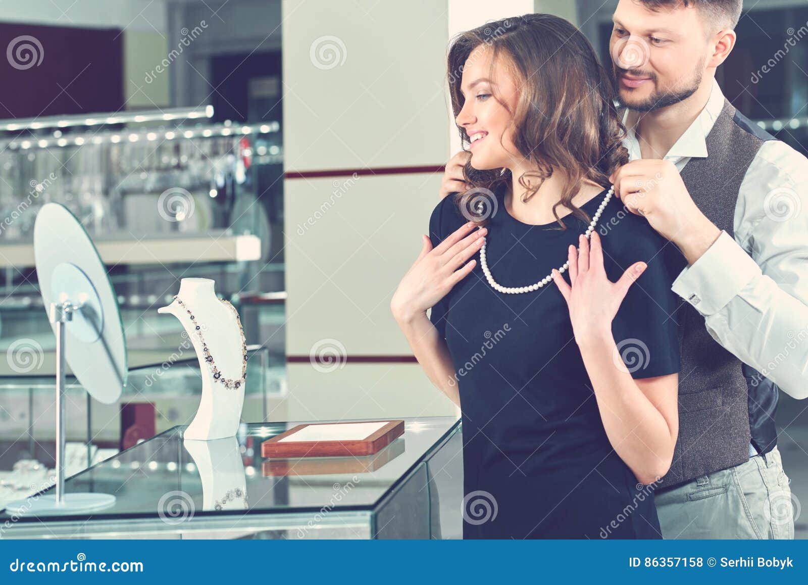 Young Man Helping His Girlfriend With Fitting Necklace At The Je Stock