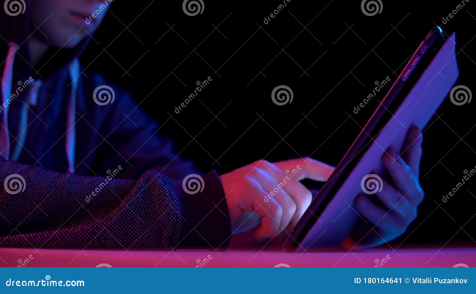 Young Man in a Hood with a Tablet. Hacker Makes a Hack through the ...