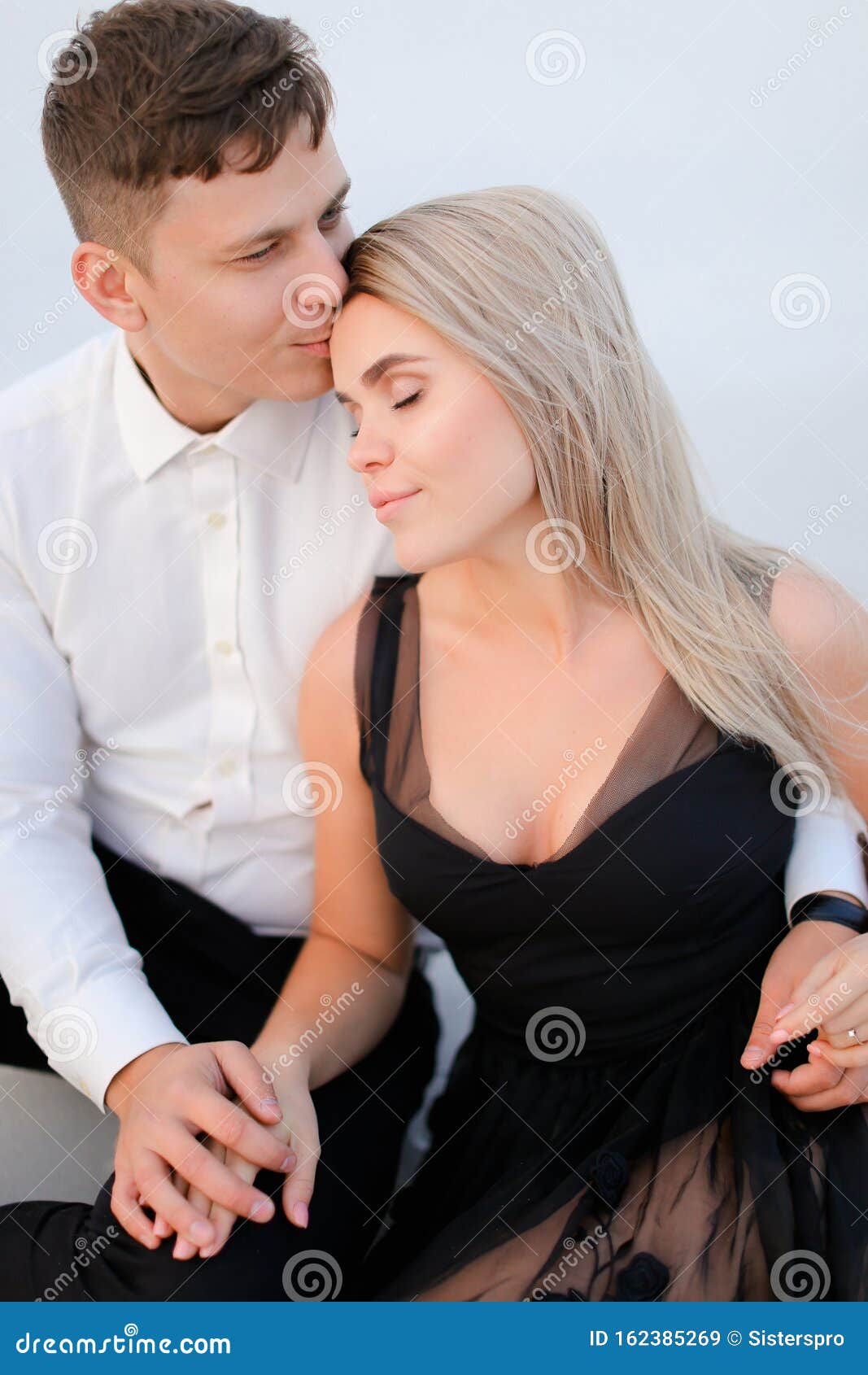 Young Man Hugging And Kissing Blonde Woman In Black Dress Stock Image