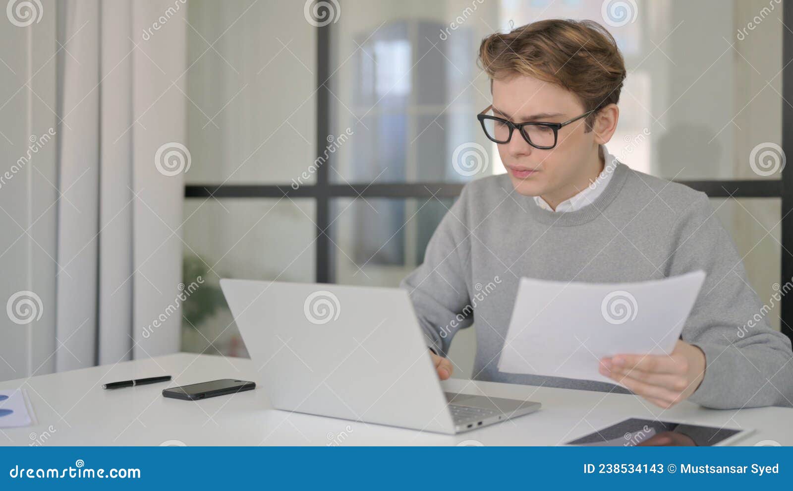 Young Man with Laptop Reading Documents in Modern Office Stock Image ...