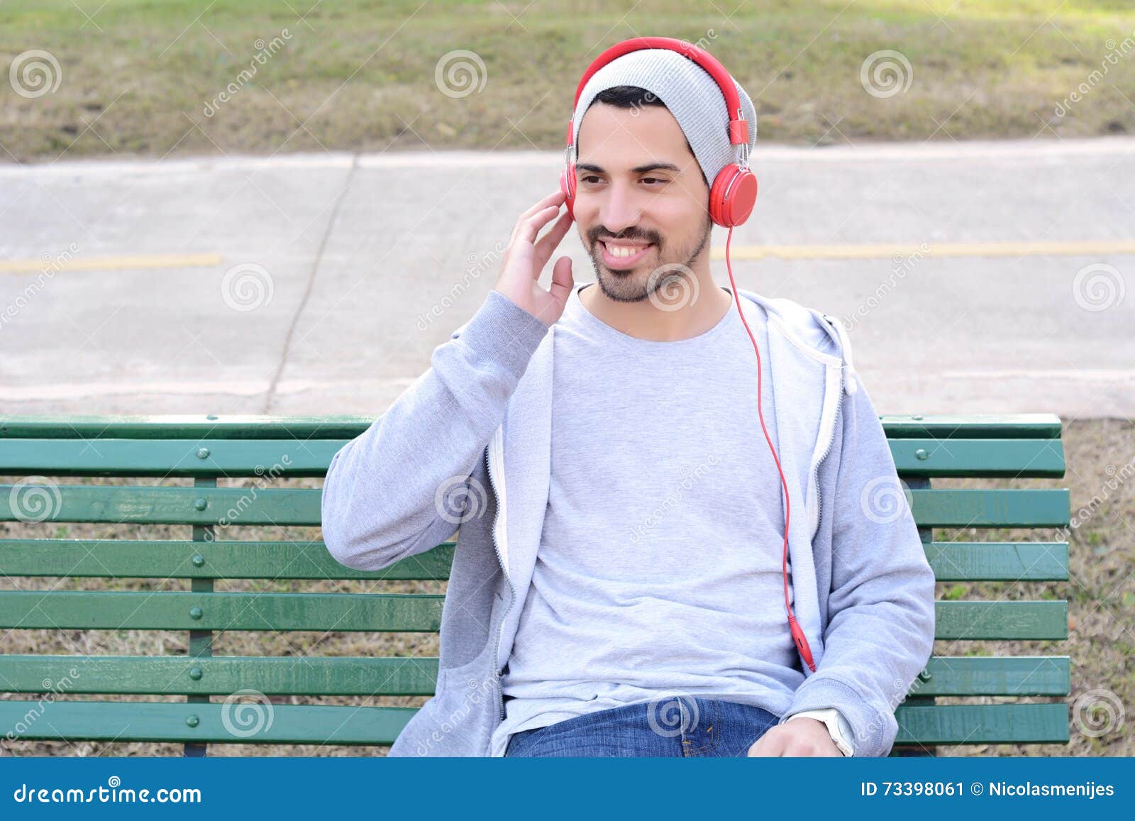 Young Man Listening To Music With Headphones Sitting On Park Ben Stock