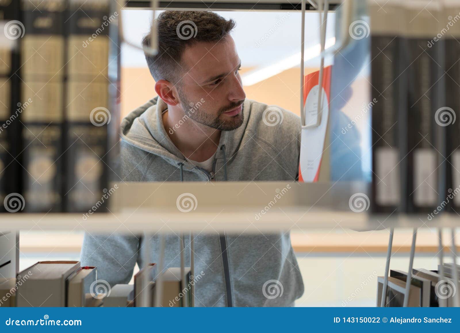 Young Man Looking for a Book on the Bookshelf of the Library Stock ...