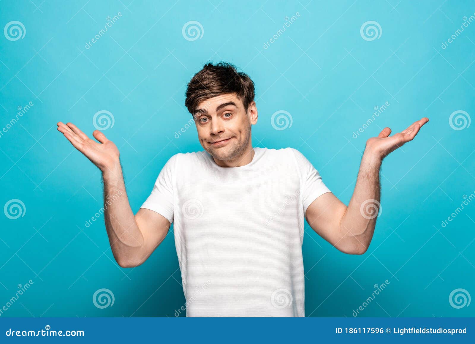 Young Man Looking at Camera and Showing Shrug Gesture on Blue ...