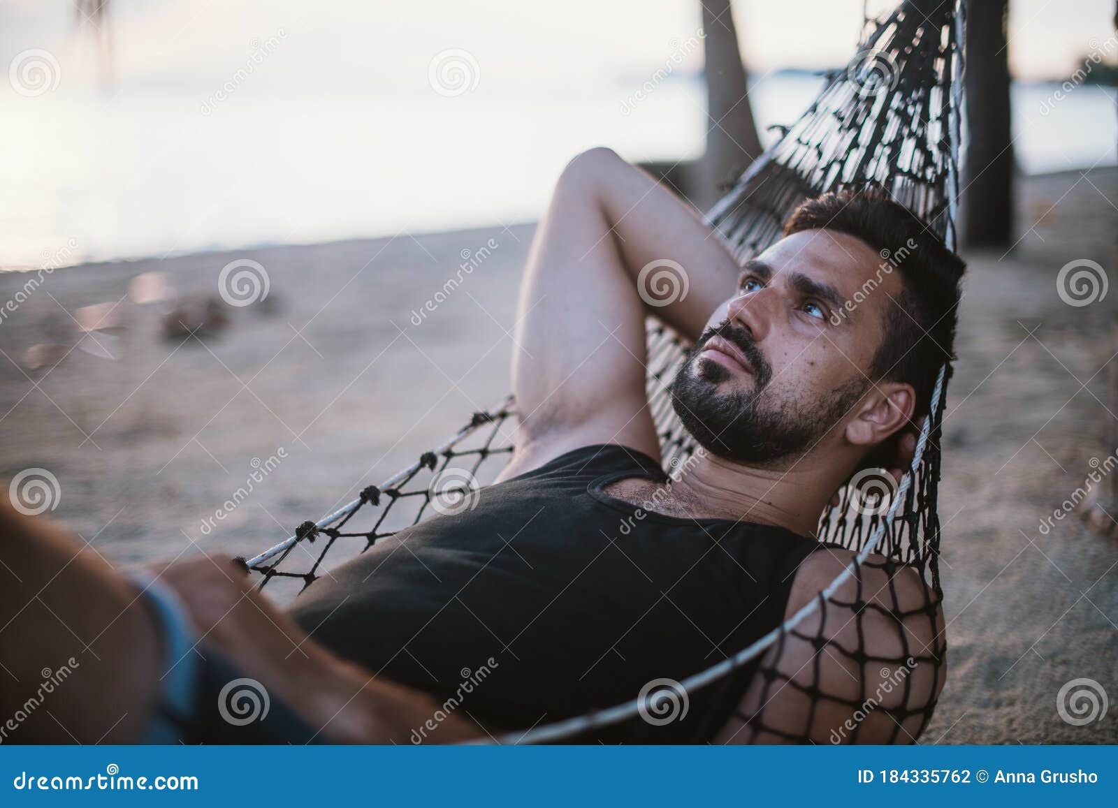 A Man is Lying in a Hammock at Sunset by the Ocean. Handsome Guy is ...