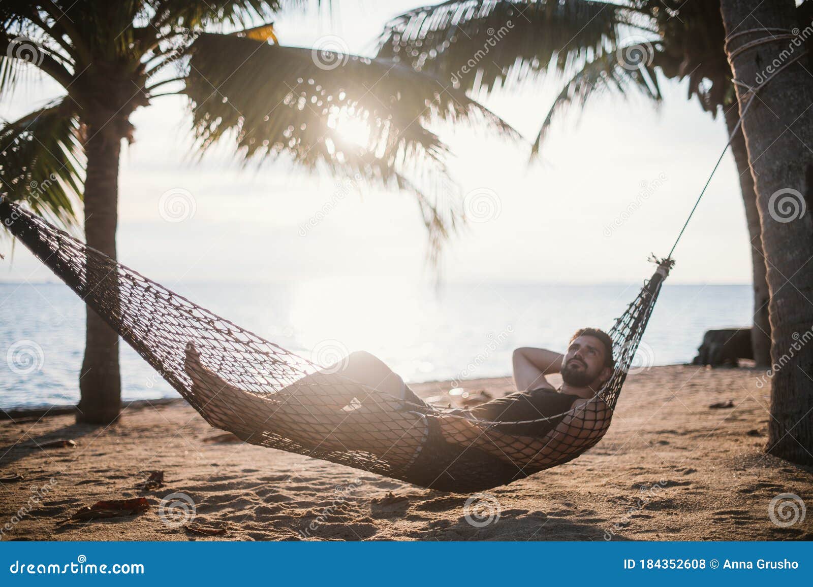 A Man is Lying in a Hammock at Sunset by the Ocean. Handsome Guy is ...