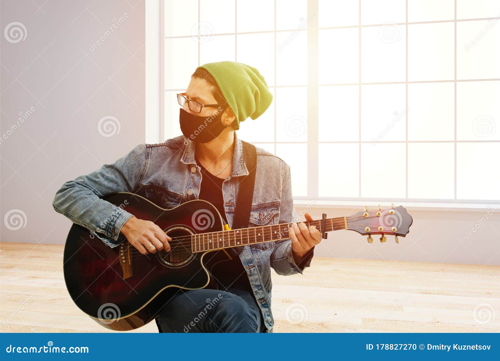 Young Man with a Mask on Face Playing the Guitar in the Light Room ...