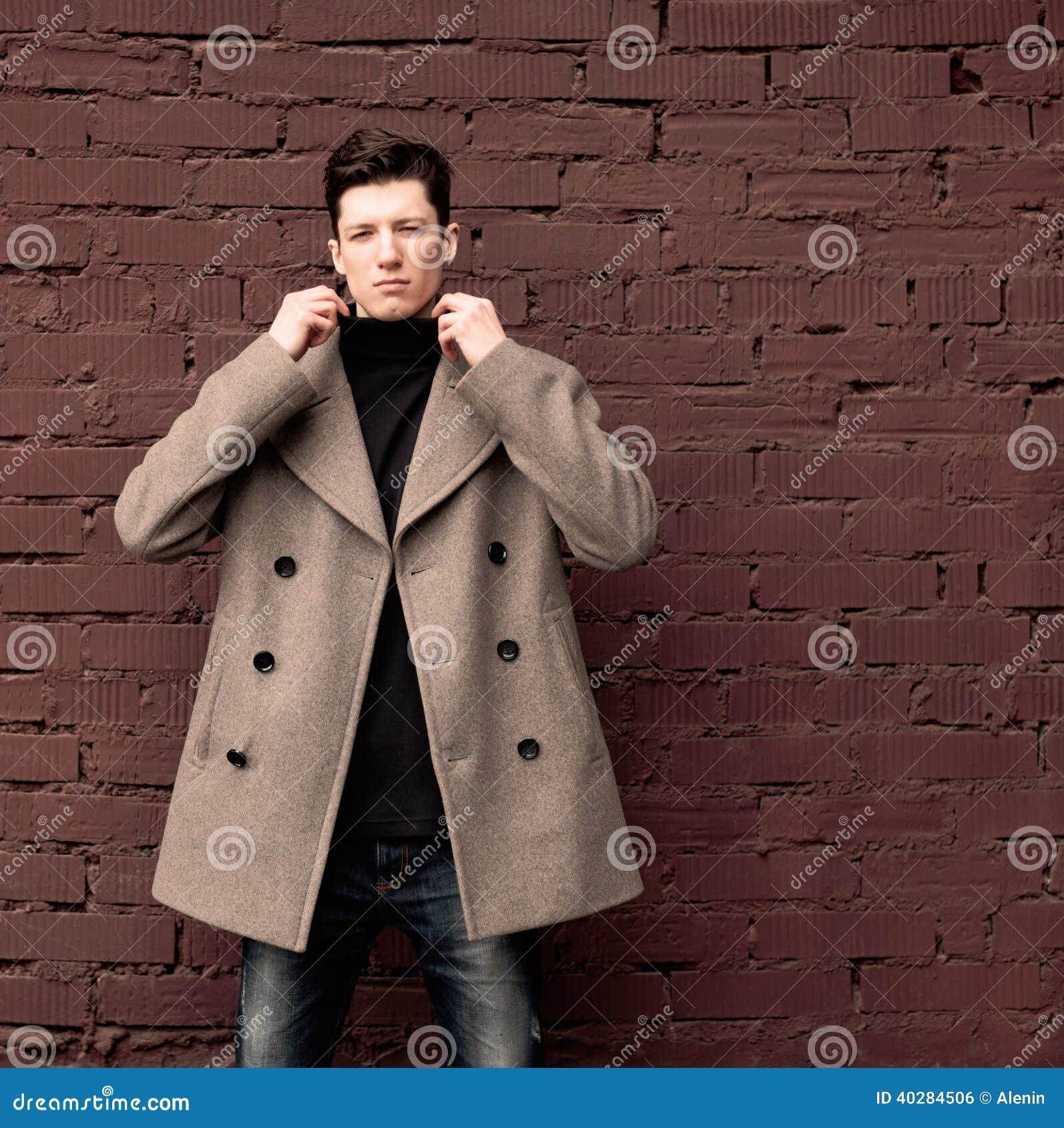 The Young Man Model in a Coat Poses at a Brick Wall. Toned Stock Photo ...