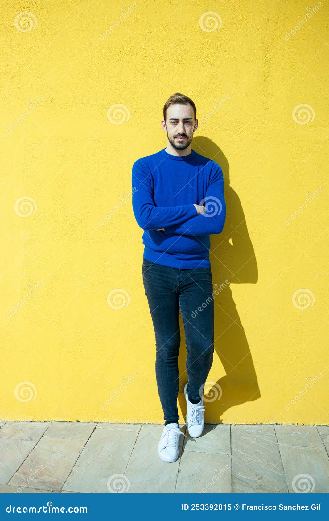 Young Man with a Neutral Expression on a Yellow Wall with Arms Crossed ...