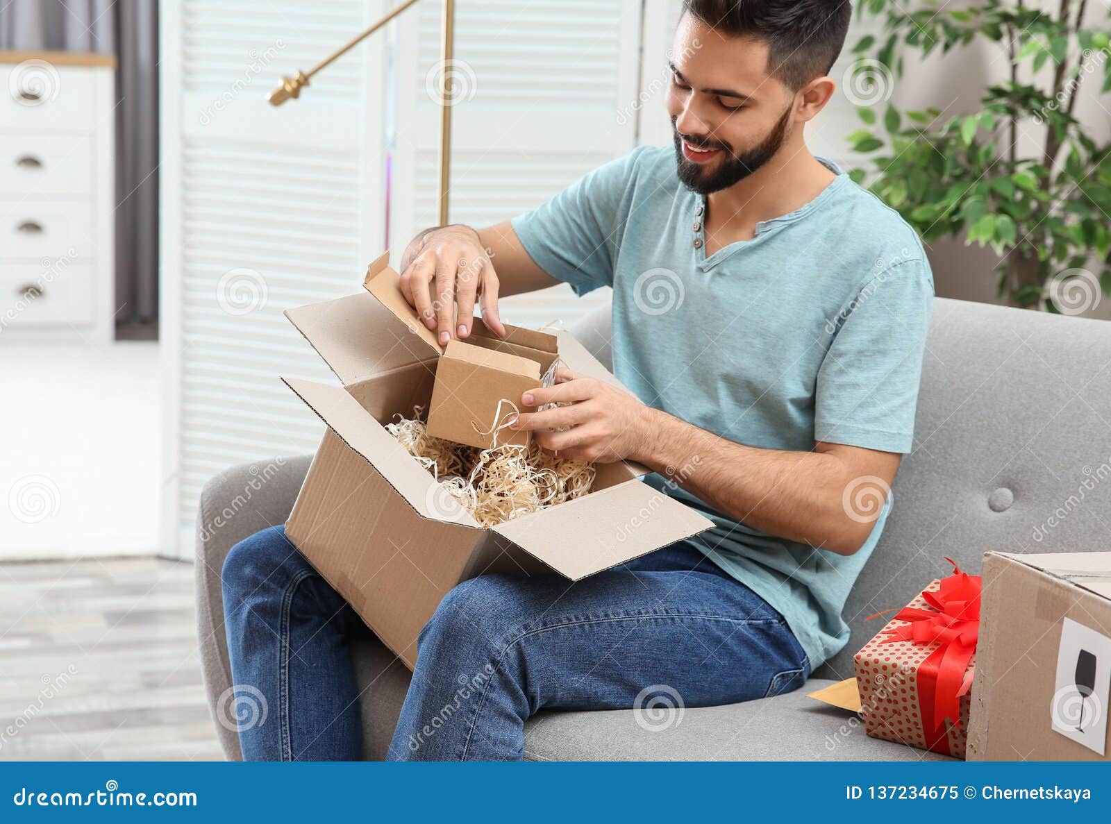 Young Man Opening Parcel on Sofa Stock Image - Image of carton ...