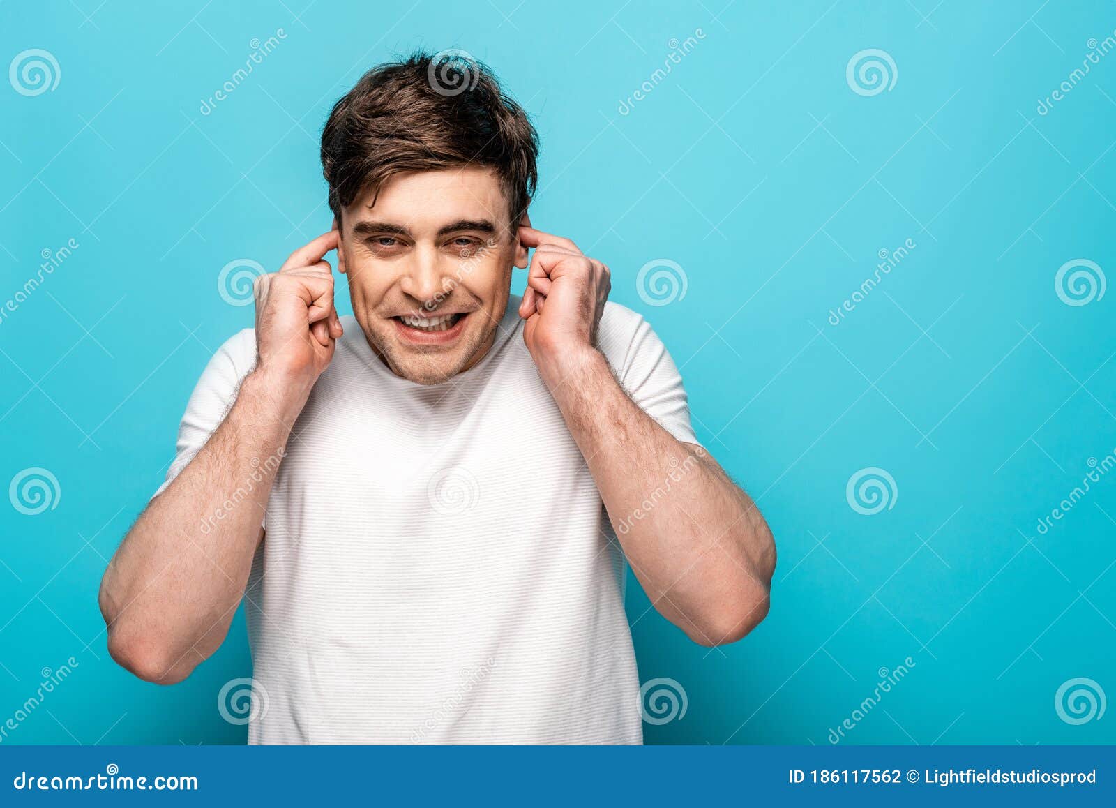 Young Man Plugging Ears with Fingers on Blue Background Stock Photo ...