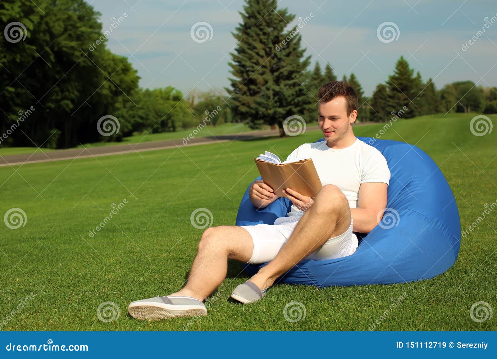 Young Man Reading Book While Sitting On Bean Bag Chair Outdoors Stock