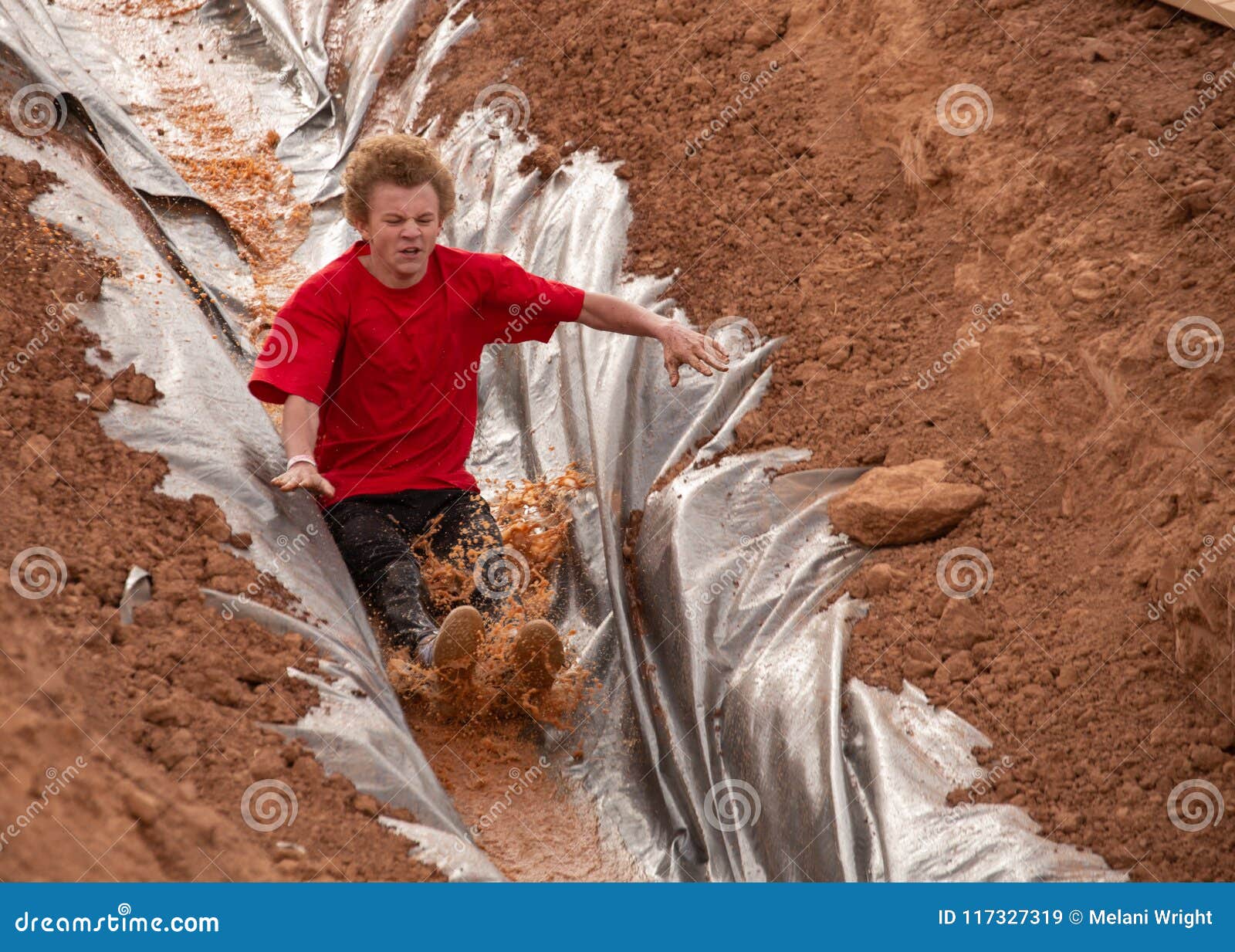 Young Man in a Red Shirt Sliding Down a Water Slide in a Mud Run ...