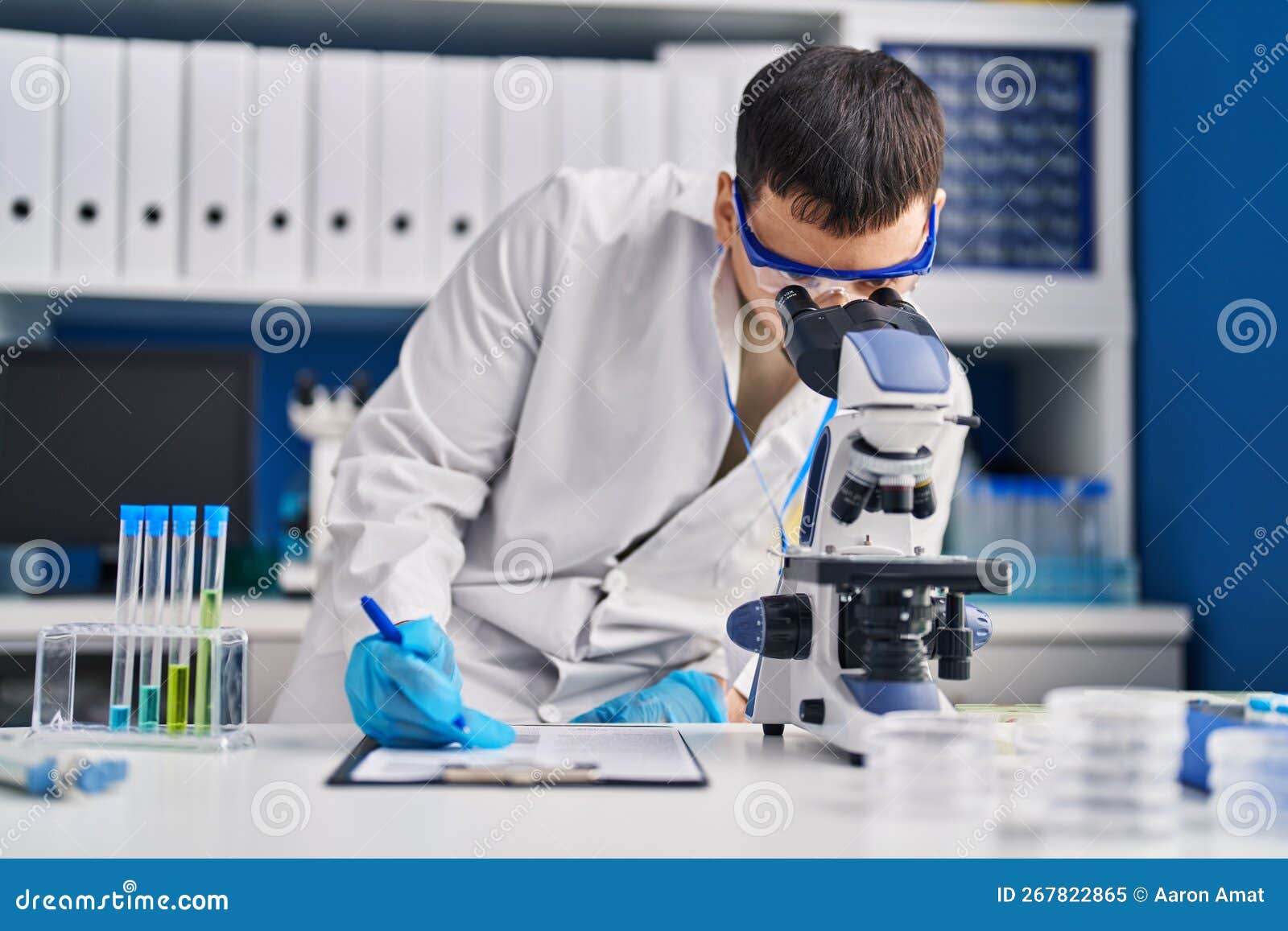 Young Man Scientist Writing on Document Using Mircoscope at Laboratory ...