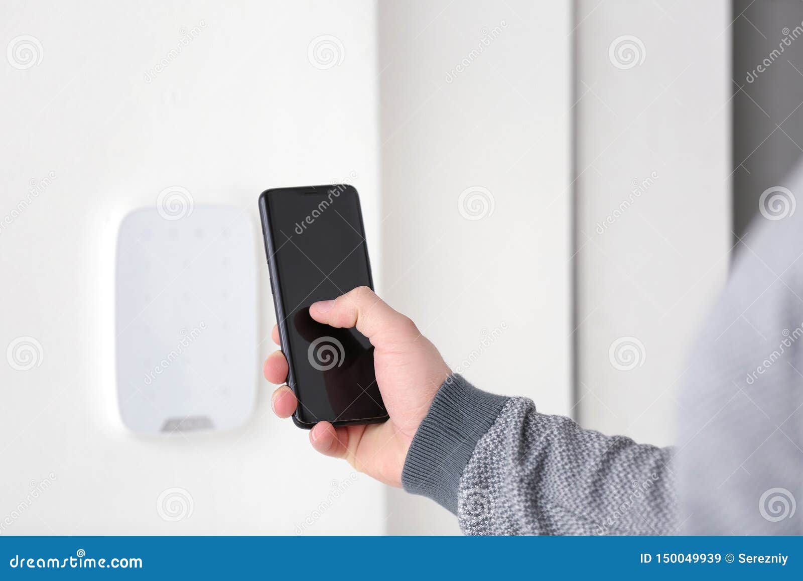 Young Man Setting Alarm System with Mobile Phone, Indoors Stock Image ...