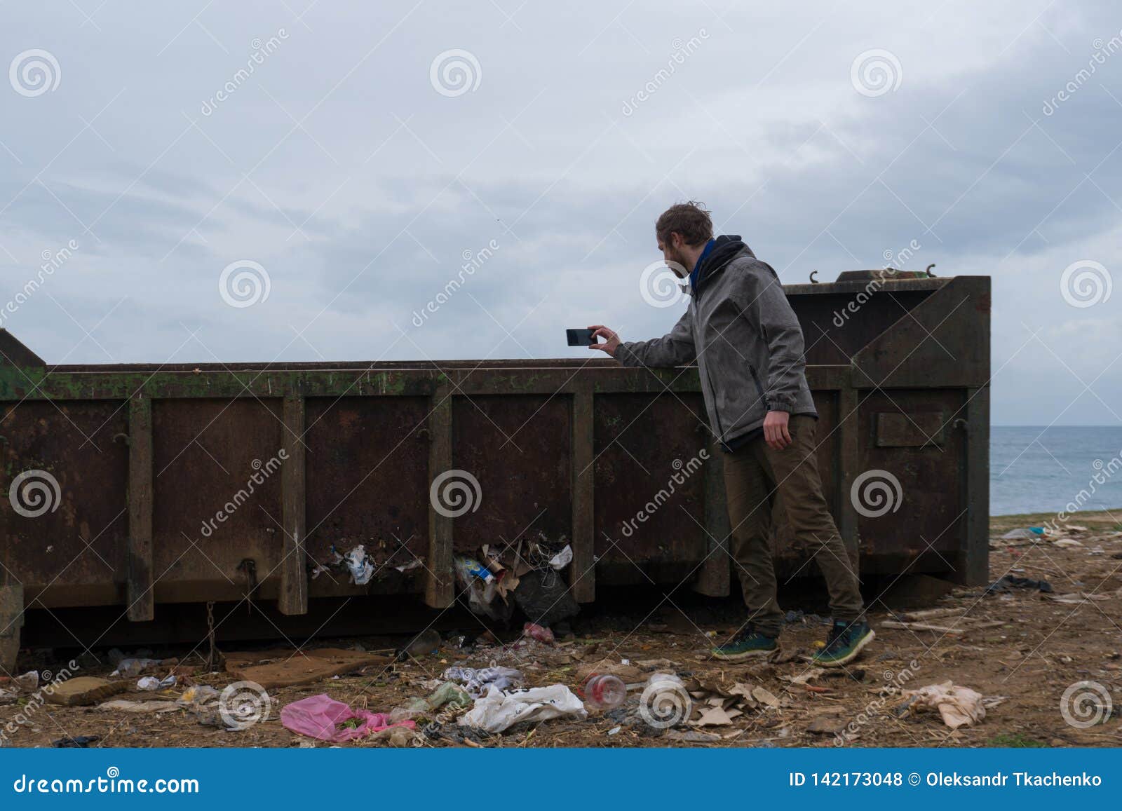 Young Man Shooting the Garbage Container with Smartphone. Littered ...