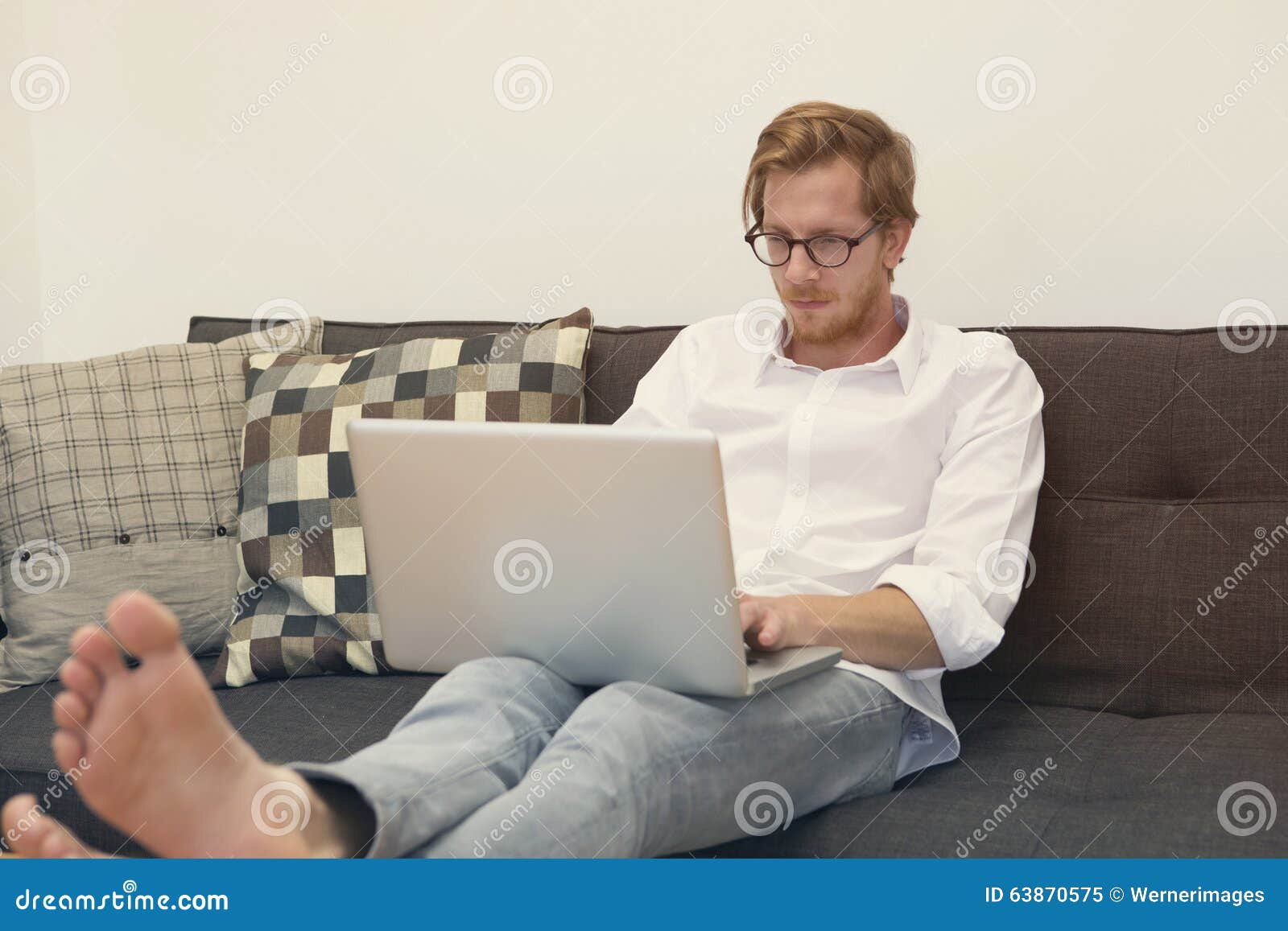 Young Man Sitting Barefoot on Couch with Laptop Stock Image - Image of ...