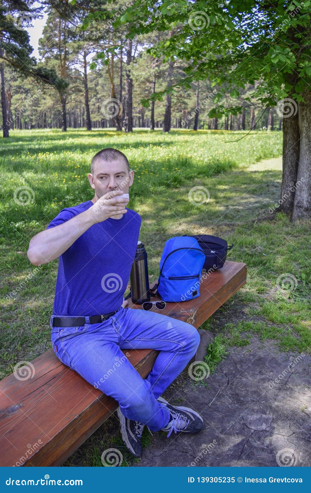 A Young Man Sitting on a Bench in the Park and Drinking Tea. Stock ...