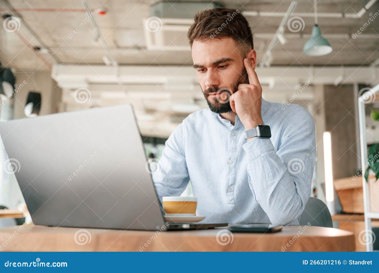 Young Man is Sitting in the Cafe and Working by Using Laptop Stock ...
