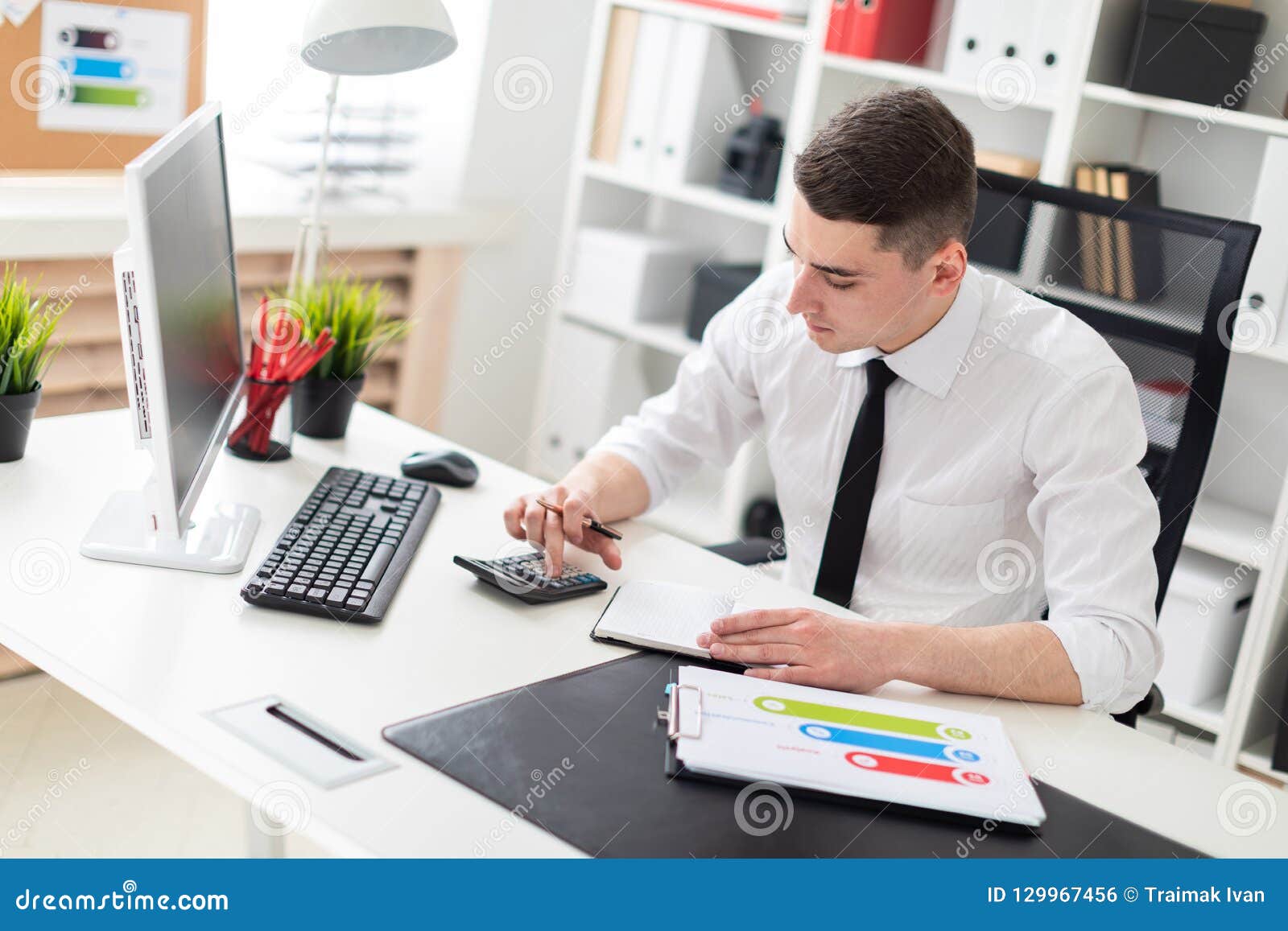 A Young Man Sitting at a Computer Desk in the Office and Working with ...